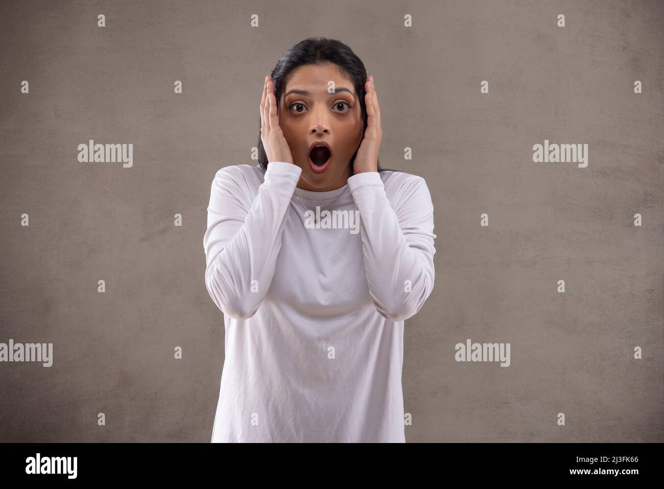 Portrait of a surprised young woman looking at camera with her both ...