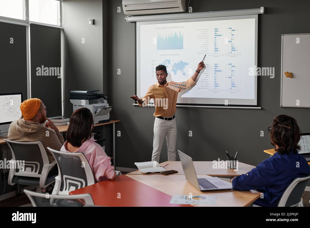 Young Black manager pointing at projection screen and presenting graphs ...