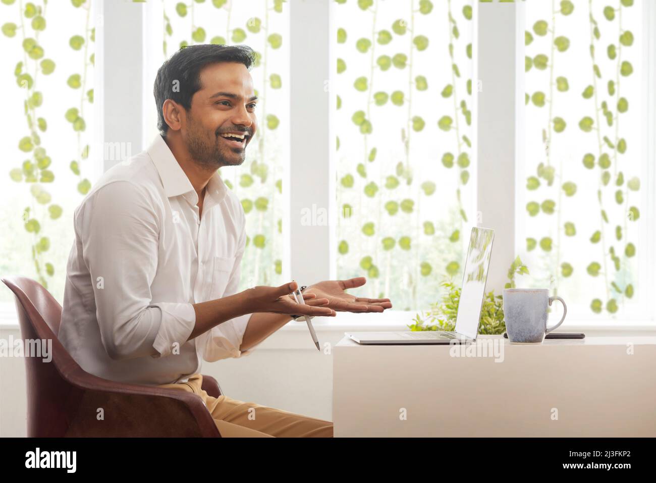 Portrait of a happy young employee smiling with gesture while sitting ...