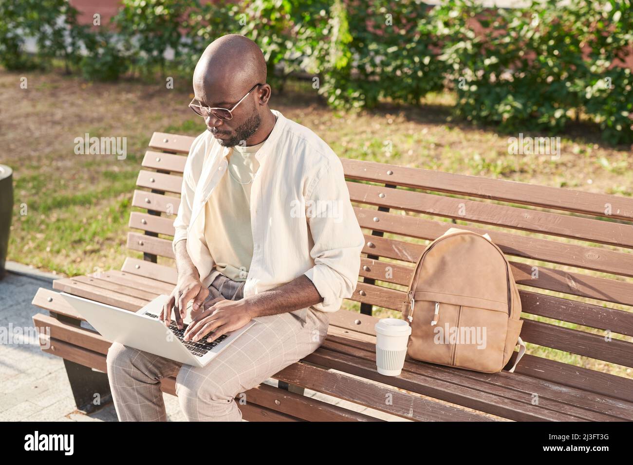 Busy young African-American man with bald head sitting on bench with ...