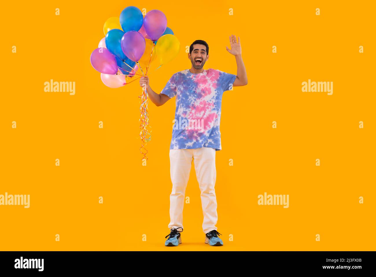 Happy young man holding bunch of balloons and gesturing with palm Stock ...