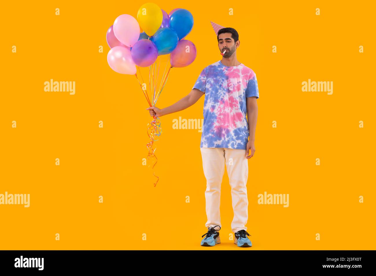 Sad young man holding balloons in hand and blowing party horn Stock ...