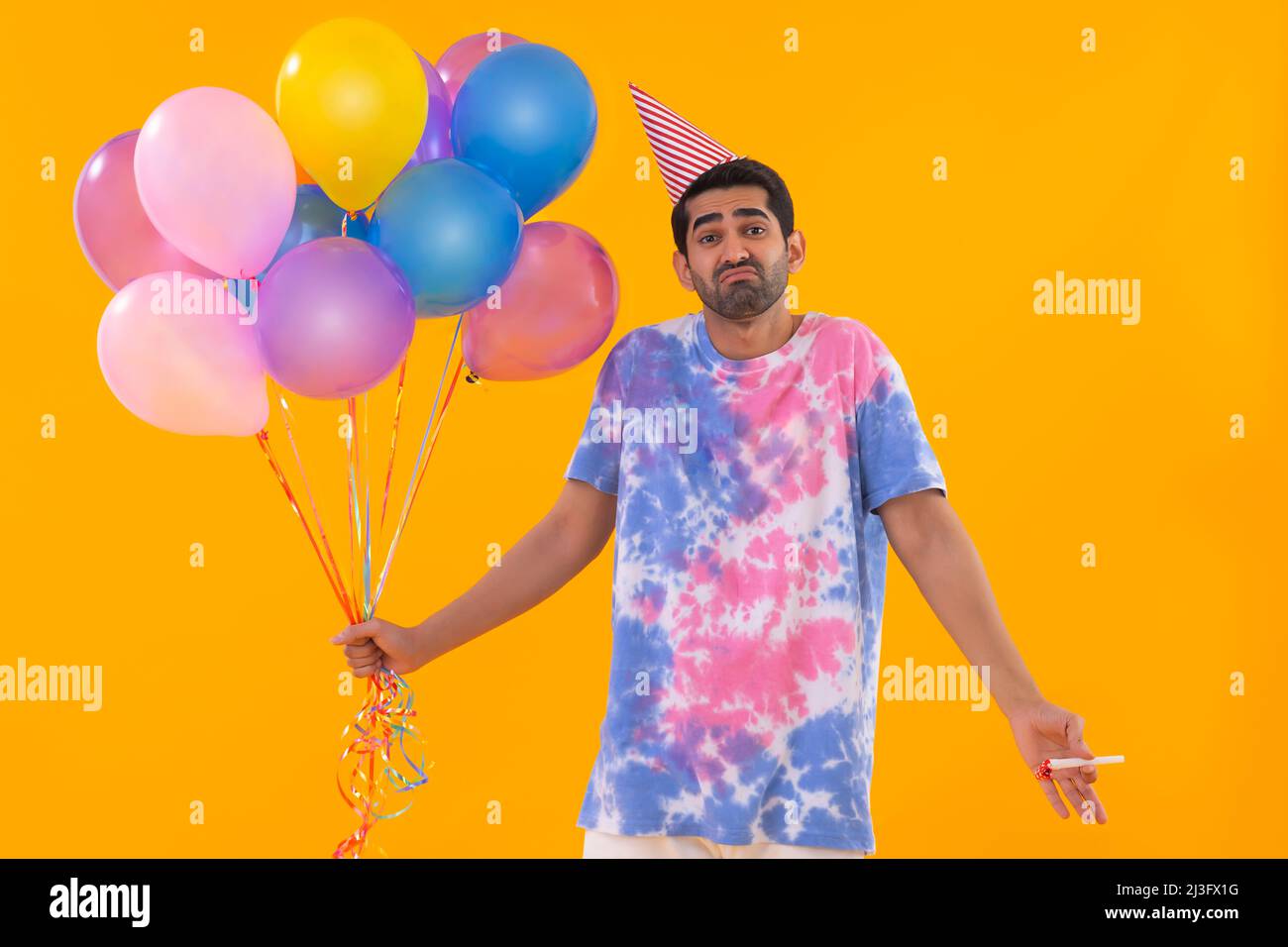 Portrait of sad young man standing with balloons and party horn in ...