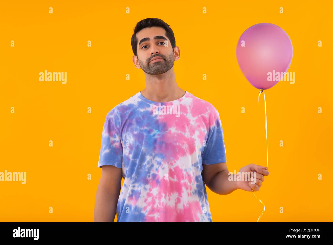 Portrait of sad young man holding balloon against yellow background ...