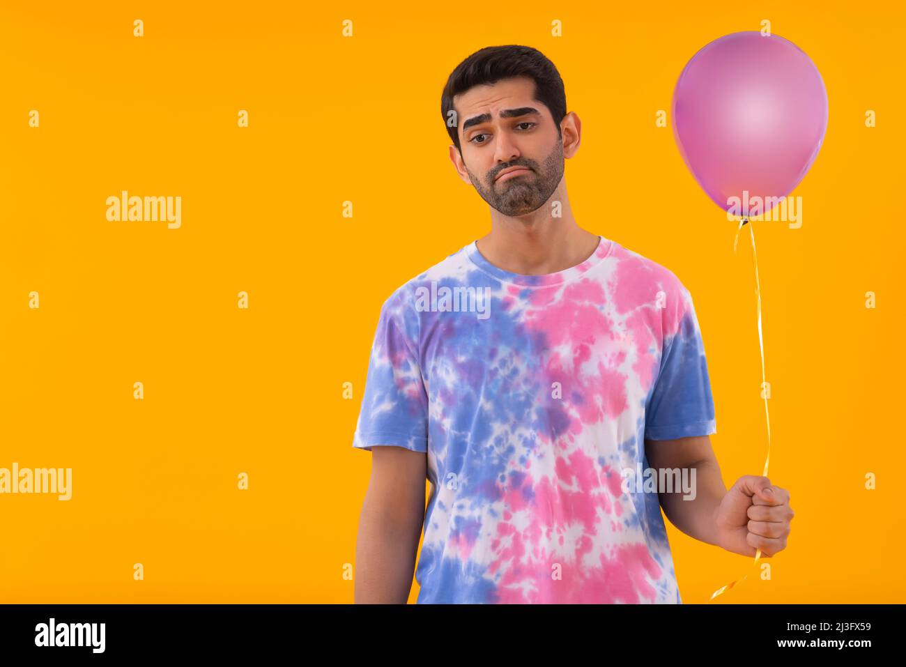 Portrait of sad young man holding balloon against yellow background ...