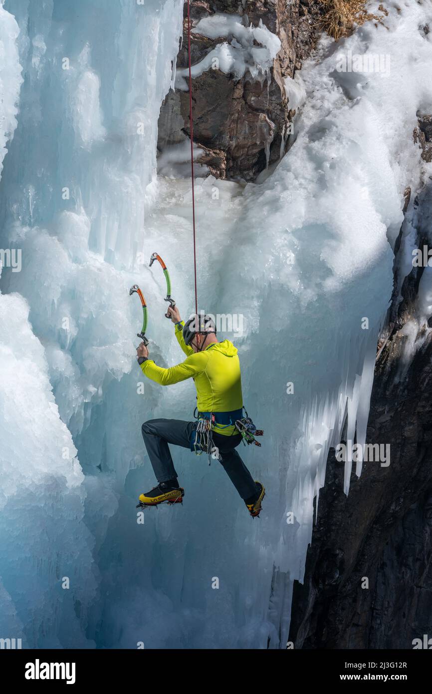An ice climber scales a 100' tall wall of ice with ice axes and ...