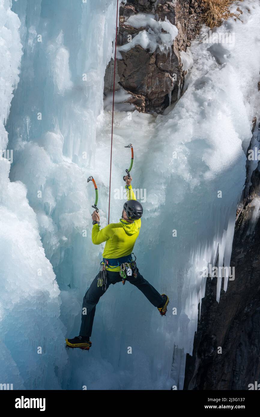 An ice climber scales a 100' tall wall of ice with ice axes and ...
