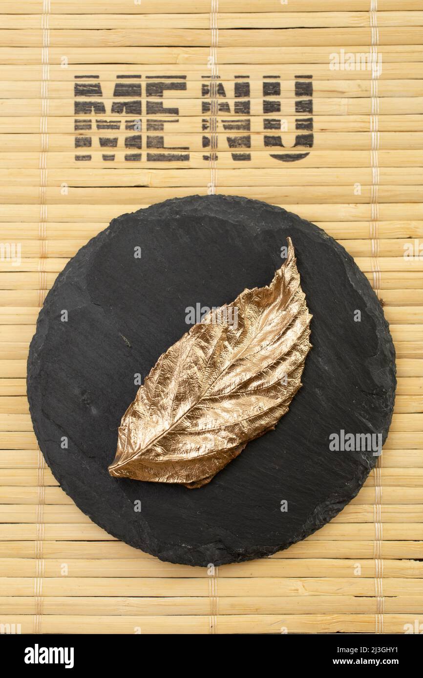 Menu word written on a bamboo placemat, with a stone tile and a golden ...