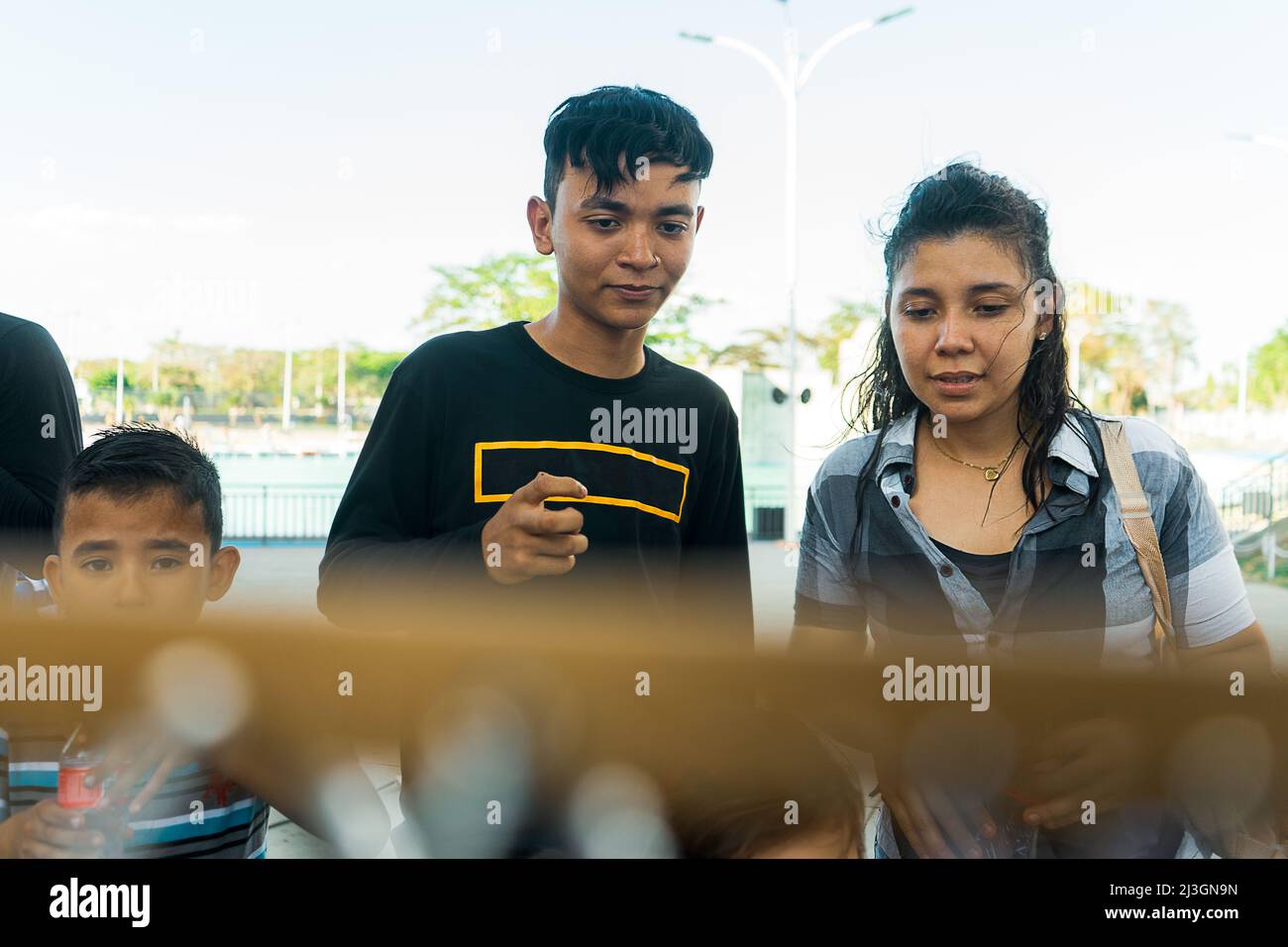 Latin brother and sister in an outdoor park trying to buy handicrafts ...