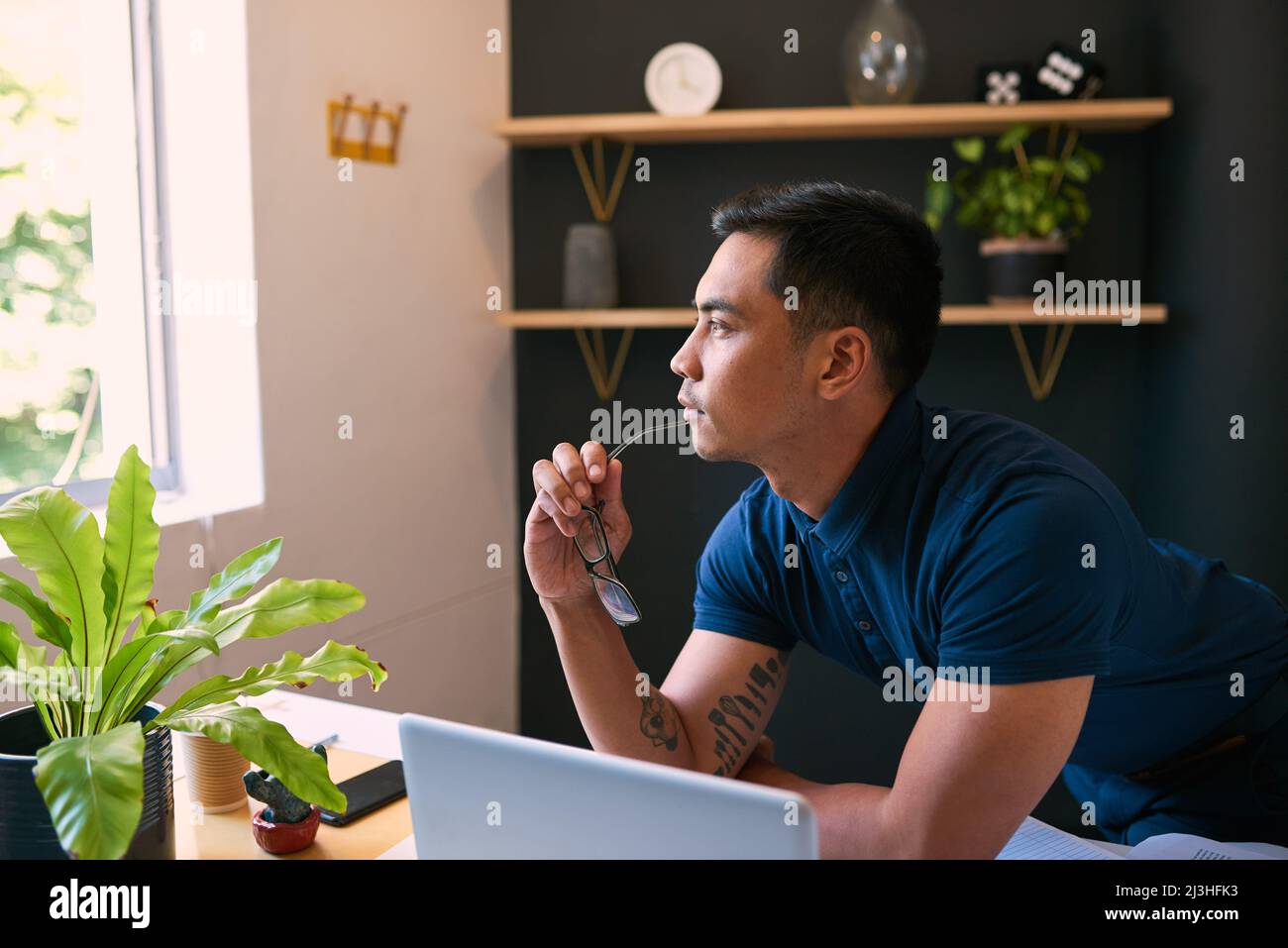 A businessman leans against his office desk and looks out the window ...