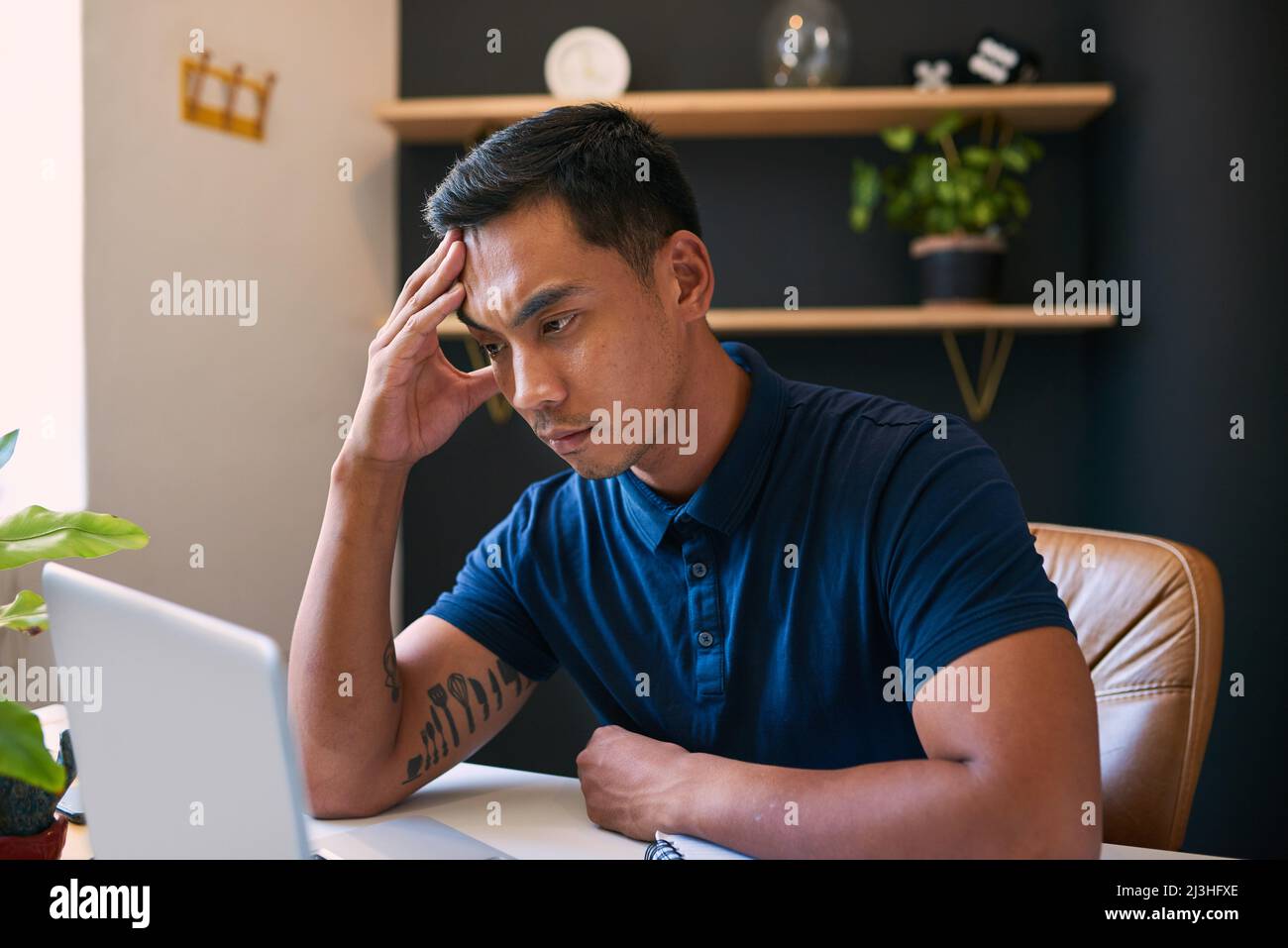 A young man frowns at his computer screen looking bored in the office ...