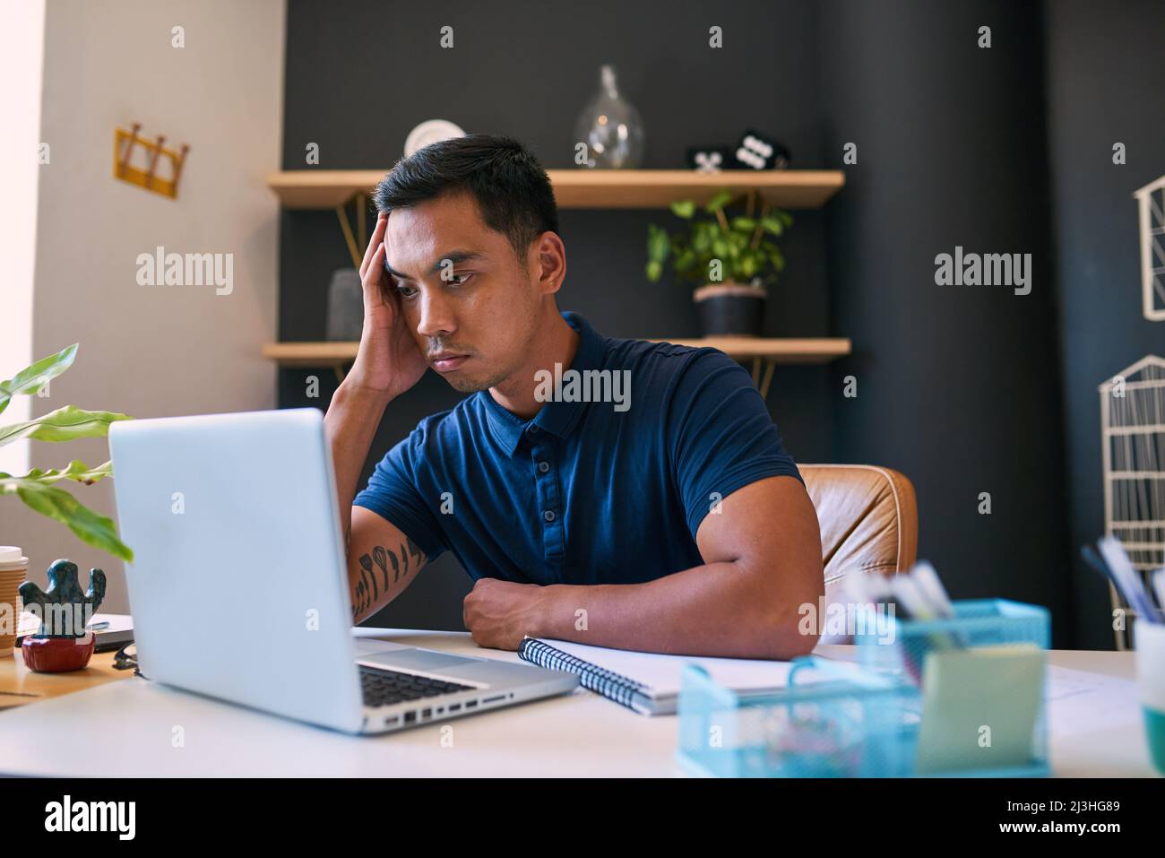 A young Asian man looks bored in the office looking at his computer ...