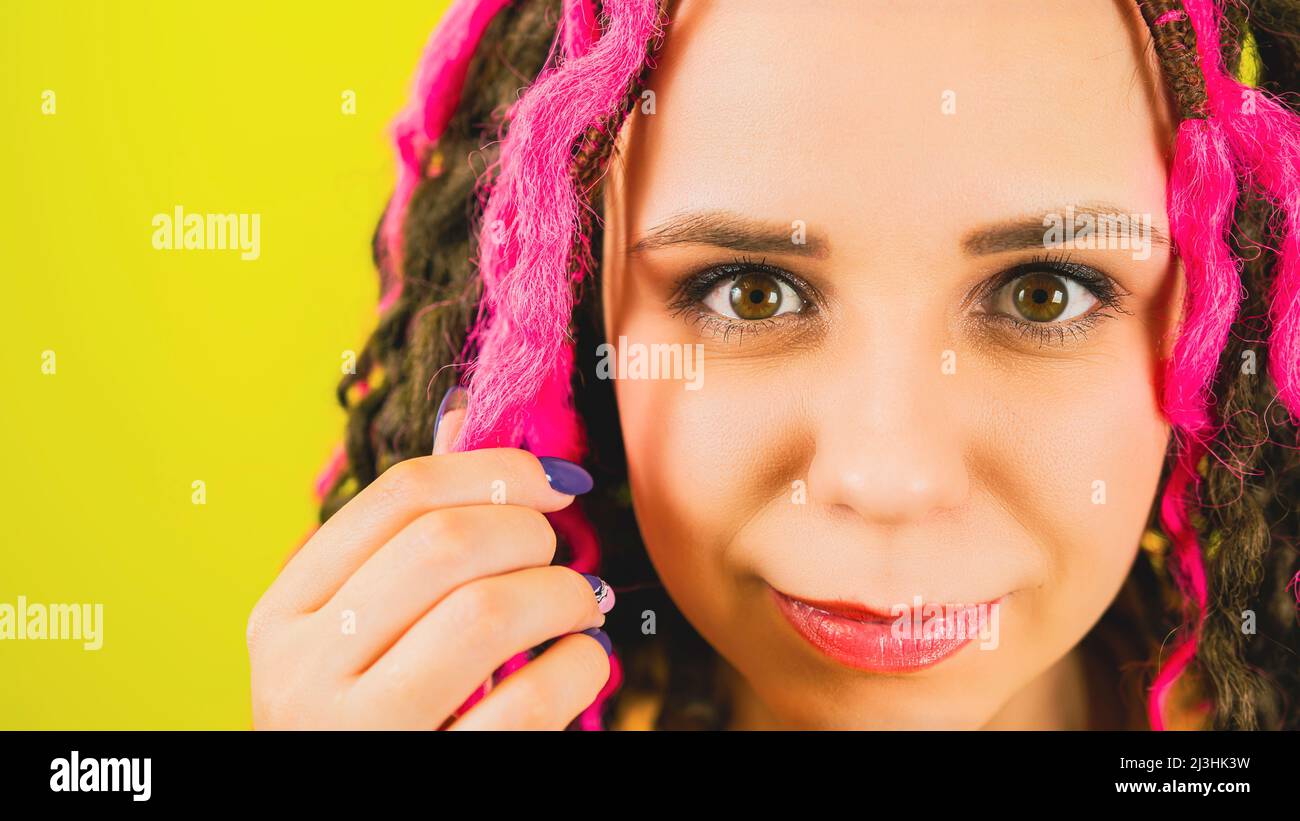Young woman twisting pink hair and looking at camera on yellow ...