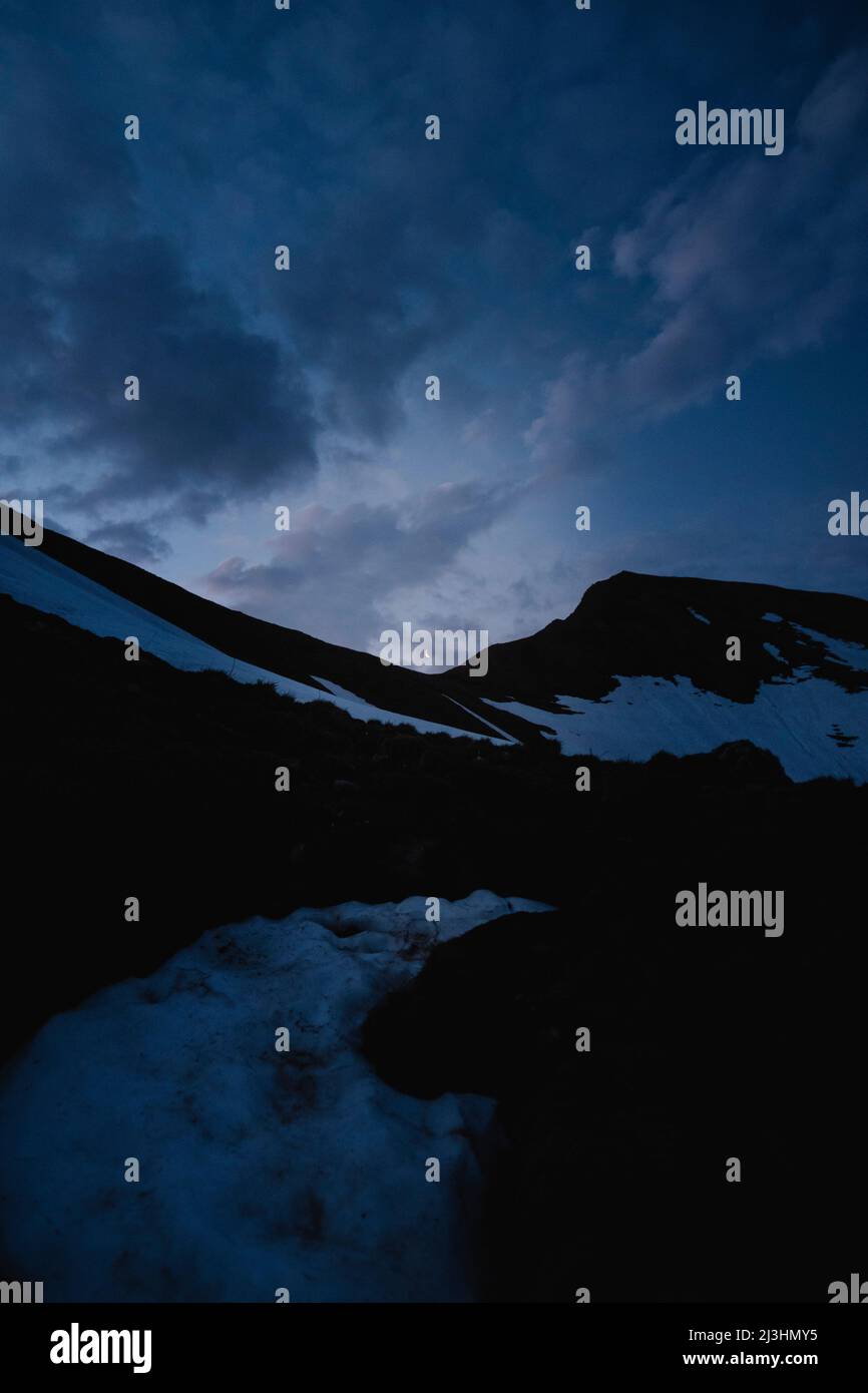 moon peaking between mountains during sunrise in snowy and mountainous ...