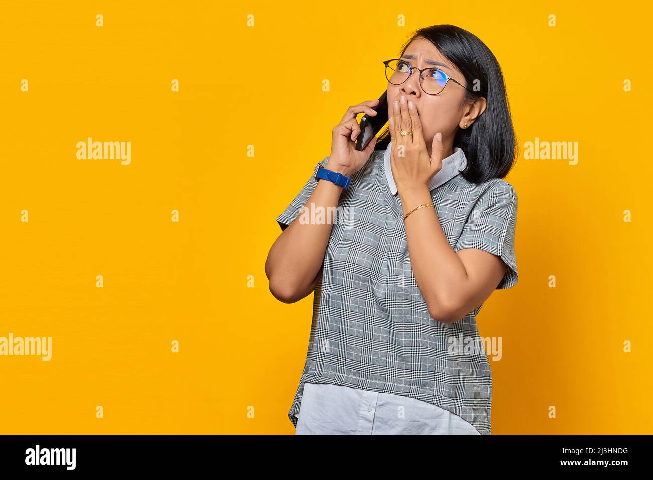 Surprised young Asian woman on receiving incoming call on mobile phone ...