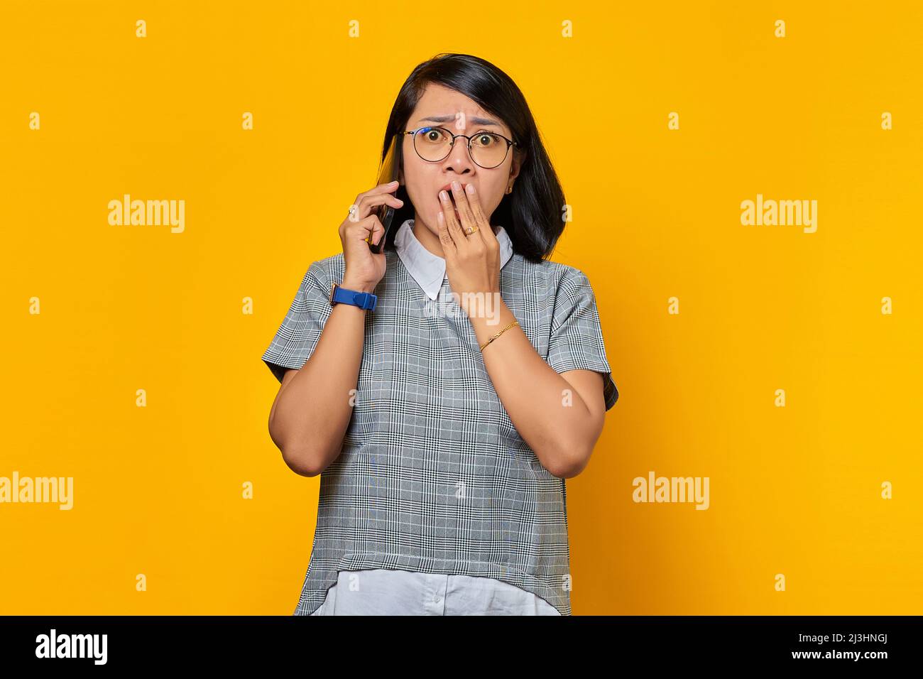 Surprised young Asian woman on receiving incoming call on mobile phone ...