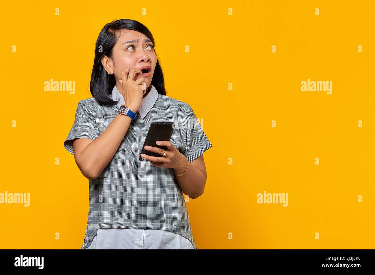 Young Asian woman holding smartphone looks anxious and worried afraid ...