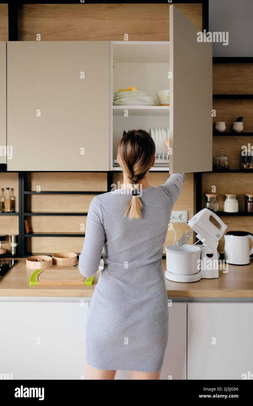 Back view young woman at home open kitchen door to take a dish while ...