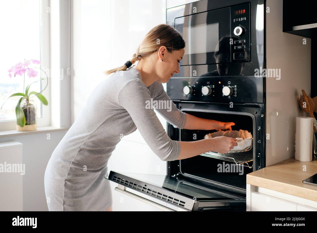 Attractive awesome girl putting baking sheet pie in oven while day ...