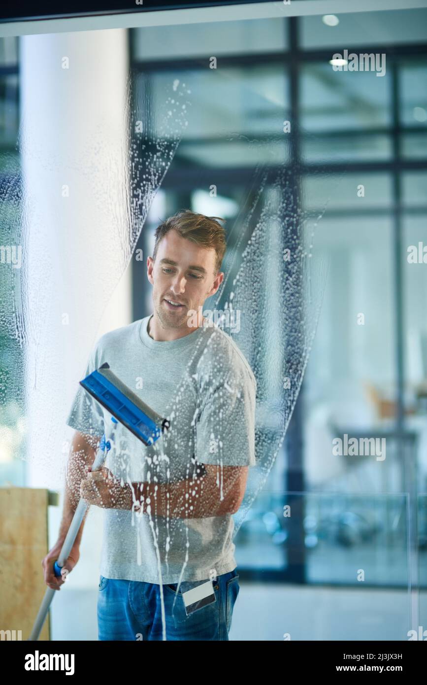 Clean windows really make an office. Shot of a young man cleaning the ...