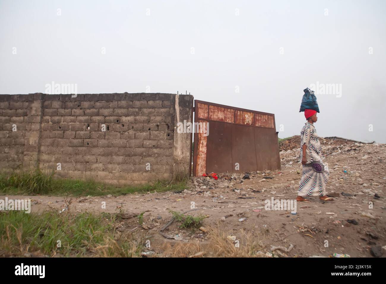 A woman with loaded bag on her head walks past a garbage dump ...