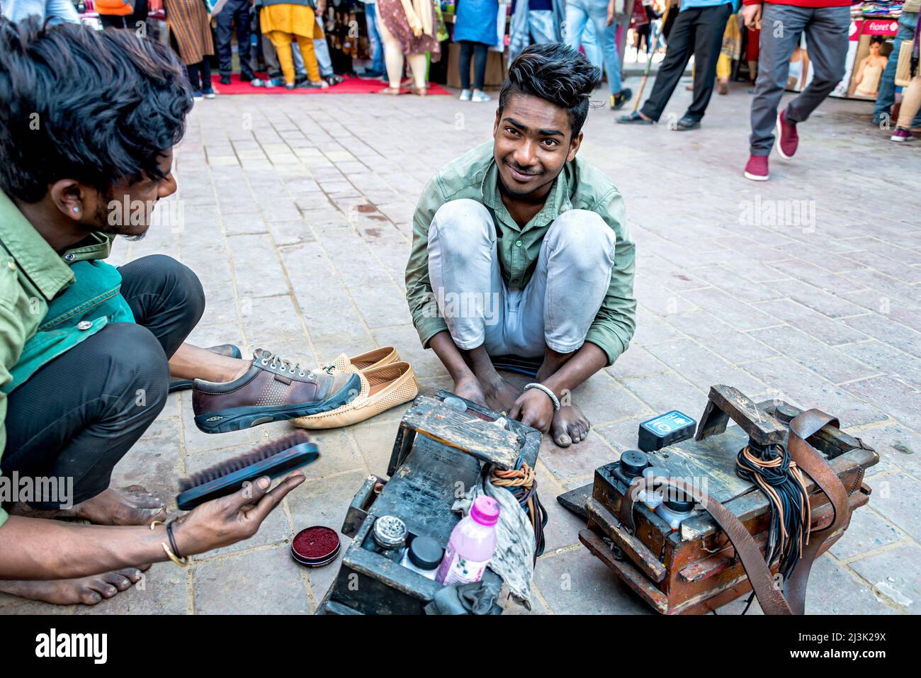 Young men crouching as they polish shoes in the street at a market in ...