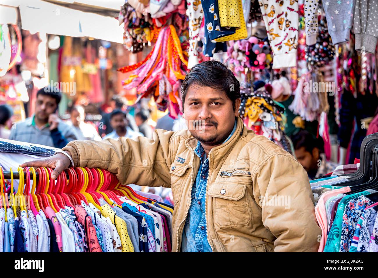 Man standing in an open air clothing stall at a market, leaning on a ...