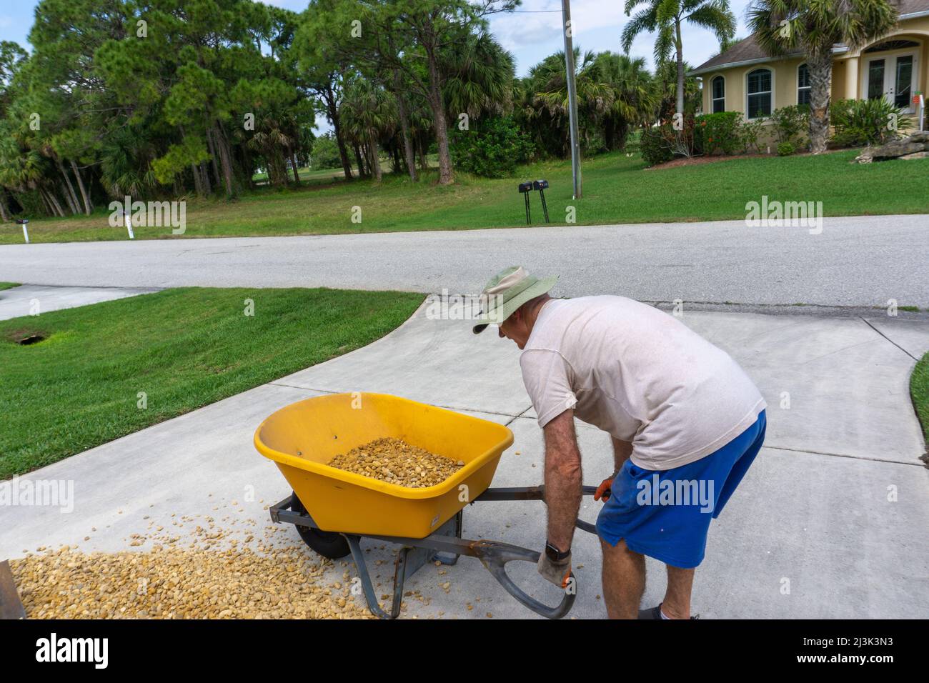 Old man bends down to pick up wheelbarrow of gravel Stock Photo - Alamy