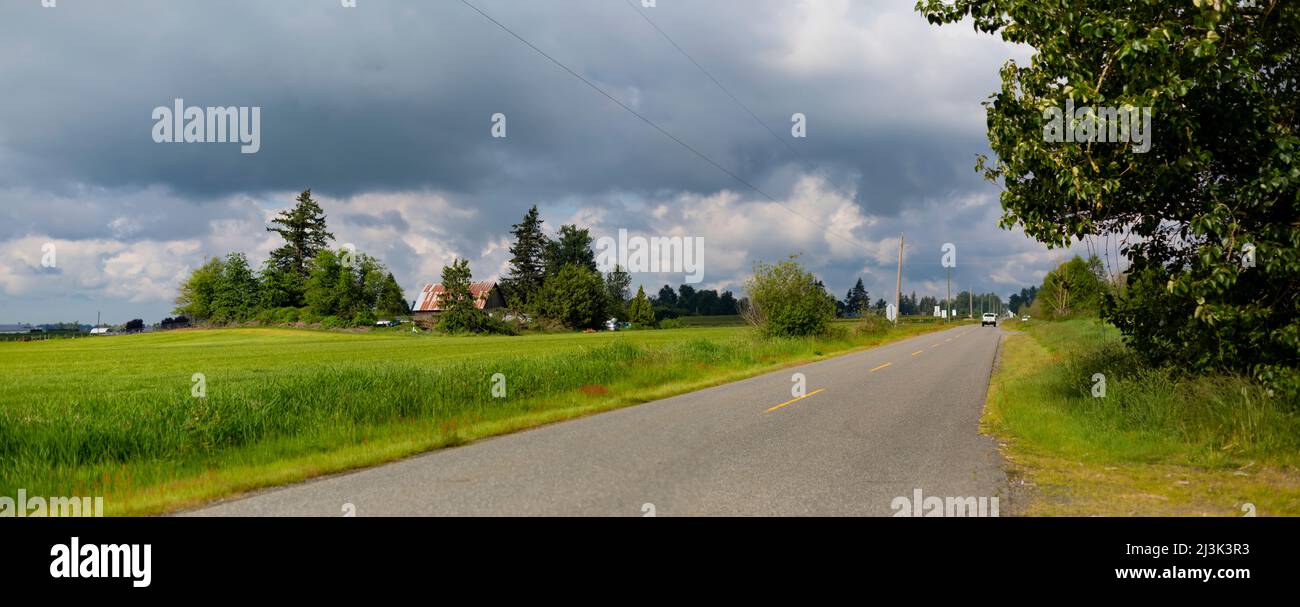 Road through farm land under a stormy sky; Abbotsford, British Columbia ...