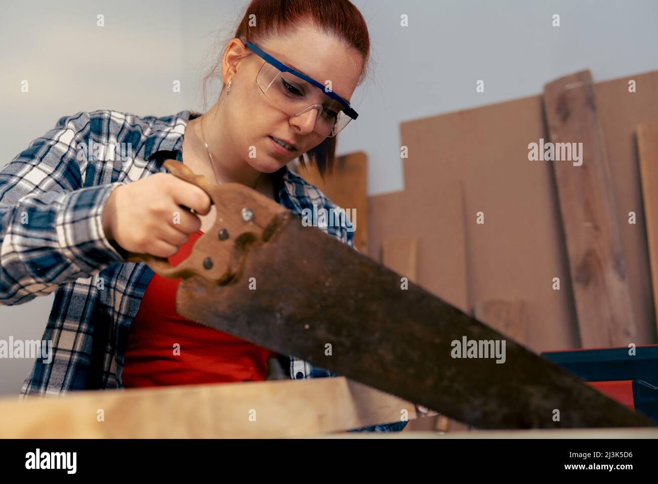 close-up of a young red-haired woman carpenter sawing a wooden board ...