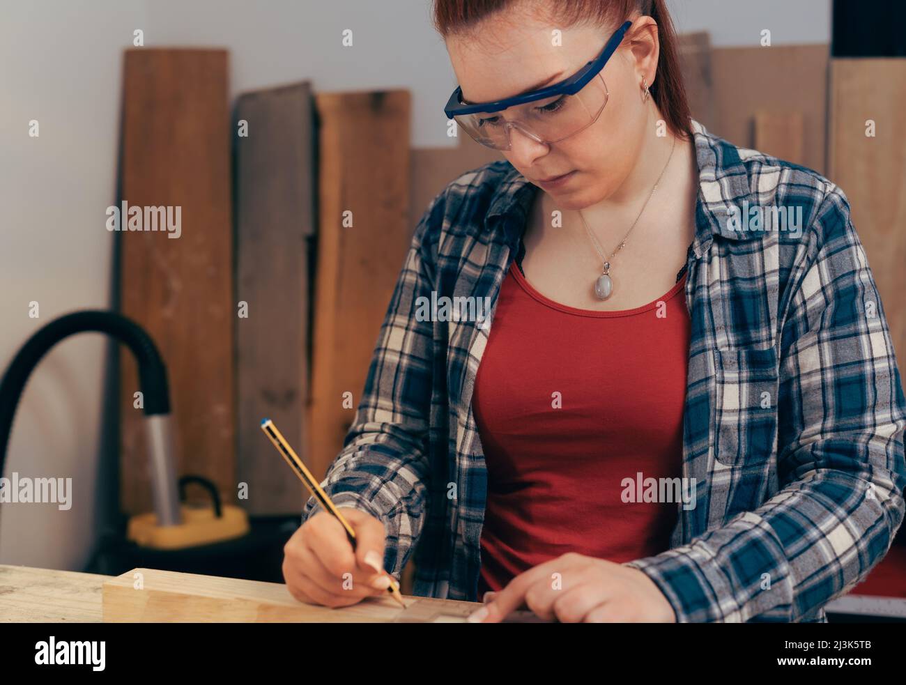 Young red haired carpenter woman, measuring a plank of wood in her ...