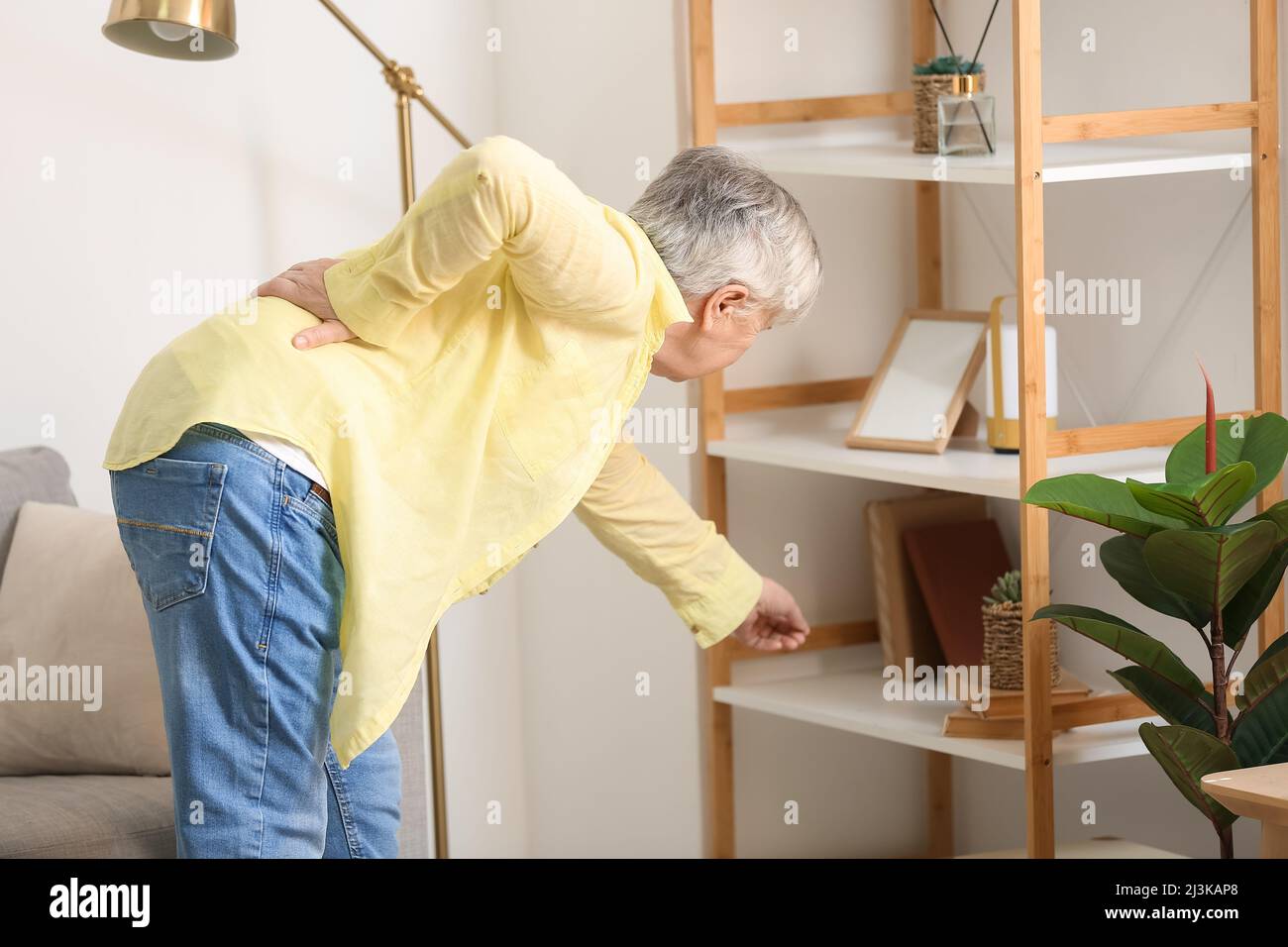 Senior woman with back pain taking book from shelf at home Stock Photo ...