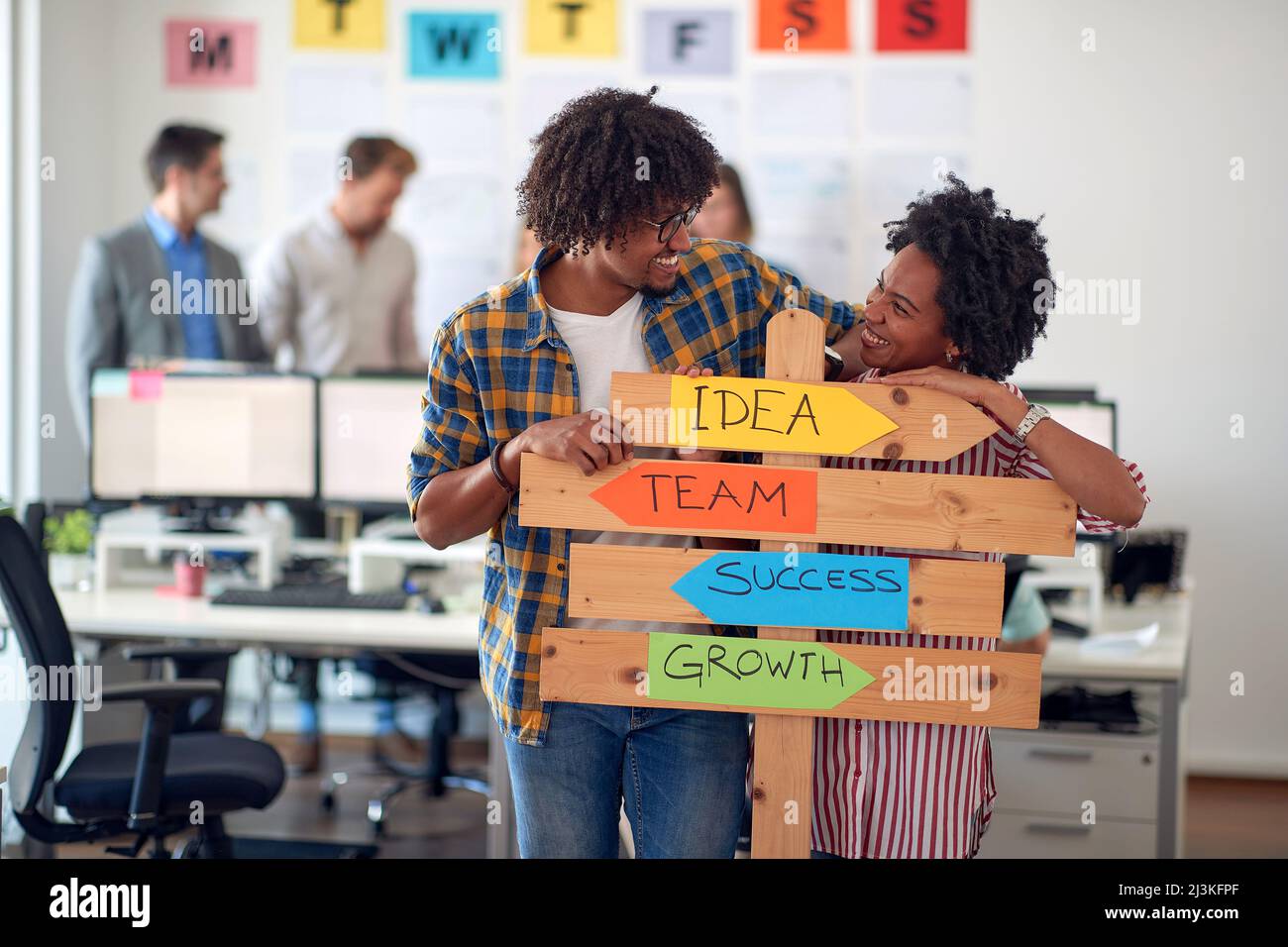 Young cheerful colleagues are holding a sign with company slogans and ...
