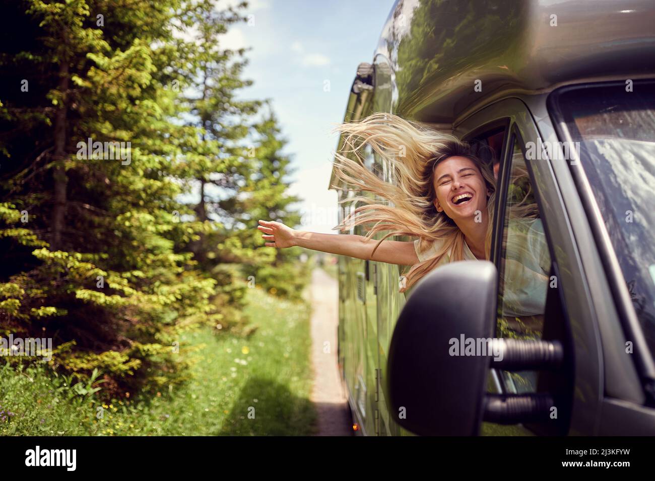 Blonde woman on the window of an rv with hands out smiling enjoying ...