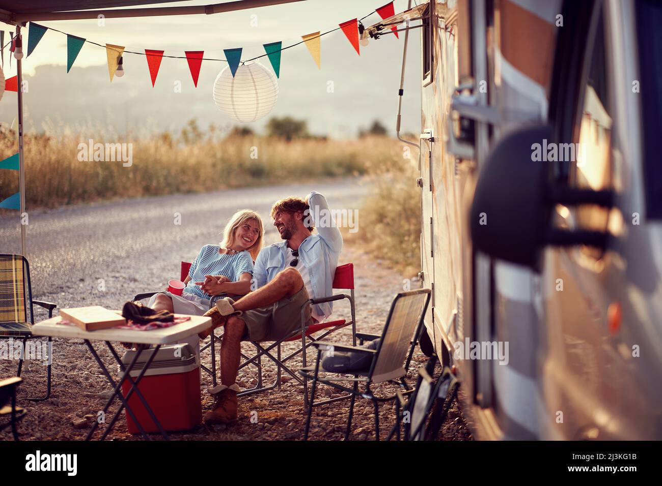 Couple in love, sitting and smilling at each other in front of camper ...