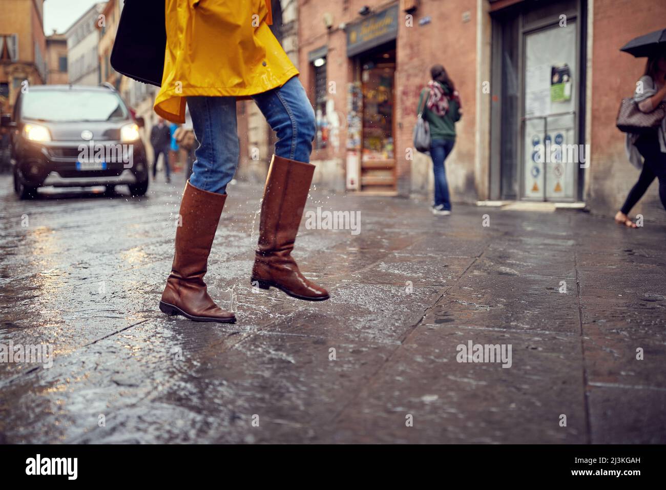 Close-up of legs of a young girl walking on the rain in the city in a ...