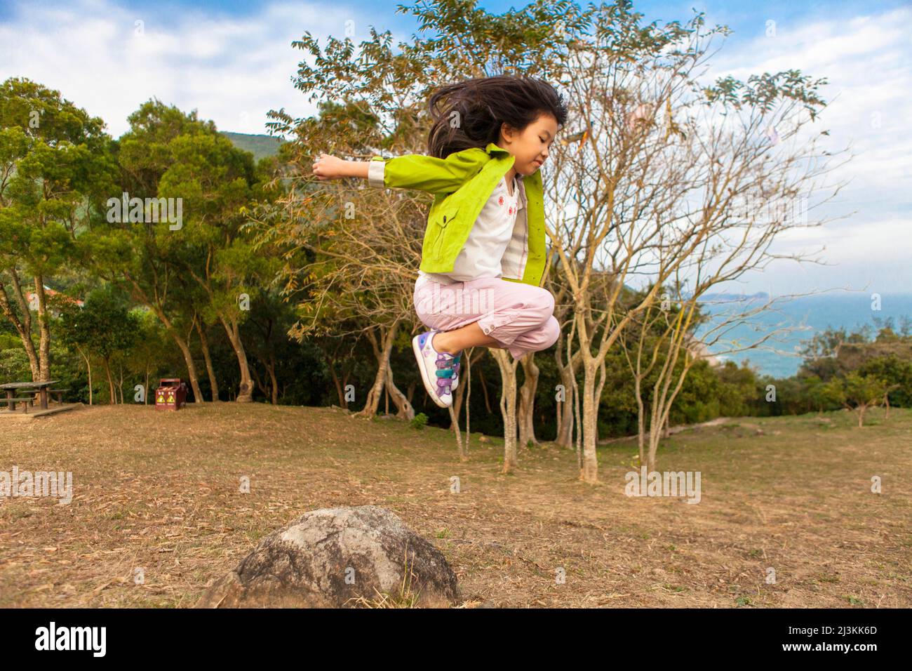 Young girl leaping over a rock in mid-air with her long hair flying out ...
