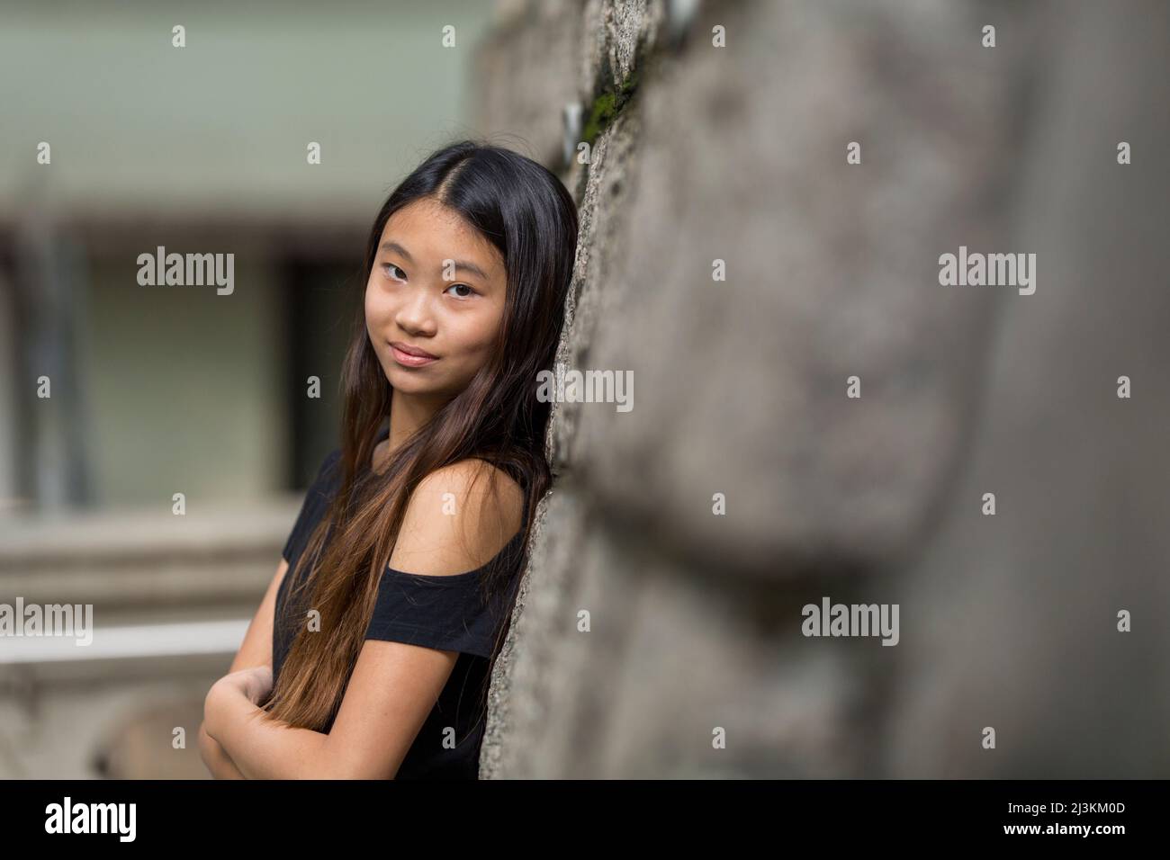 Portrait of a preteen girl leaning against a stone wall; Hong Kong ...