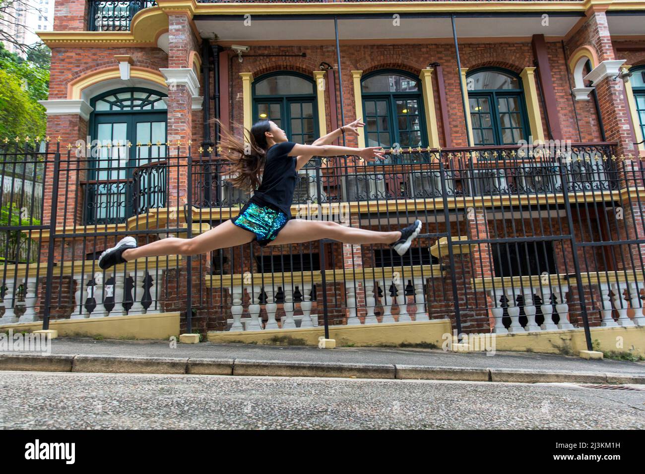 Girl leaping in mid-air in front of a building in a public park; Hong ...