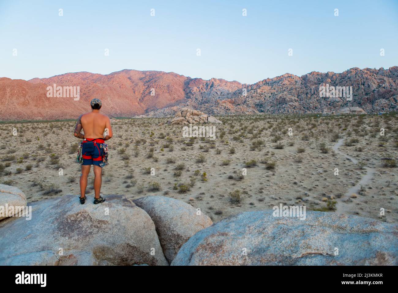 A climber watches the sunset from atop a granite block in Joshua Tree ...