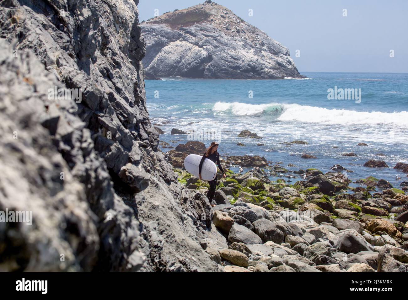 A surfer crosses a boulder strewn beach to get to the waves Stock Photo ...