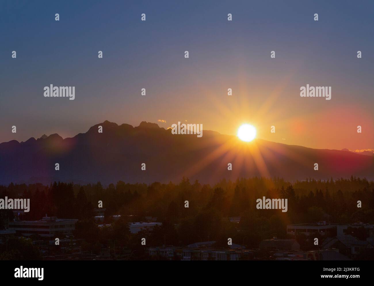Brilliant sun setting behind the mountains with sun rays flooding over ...