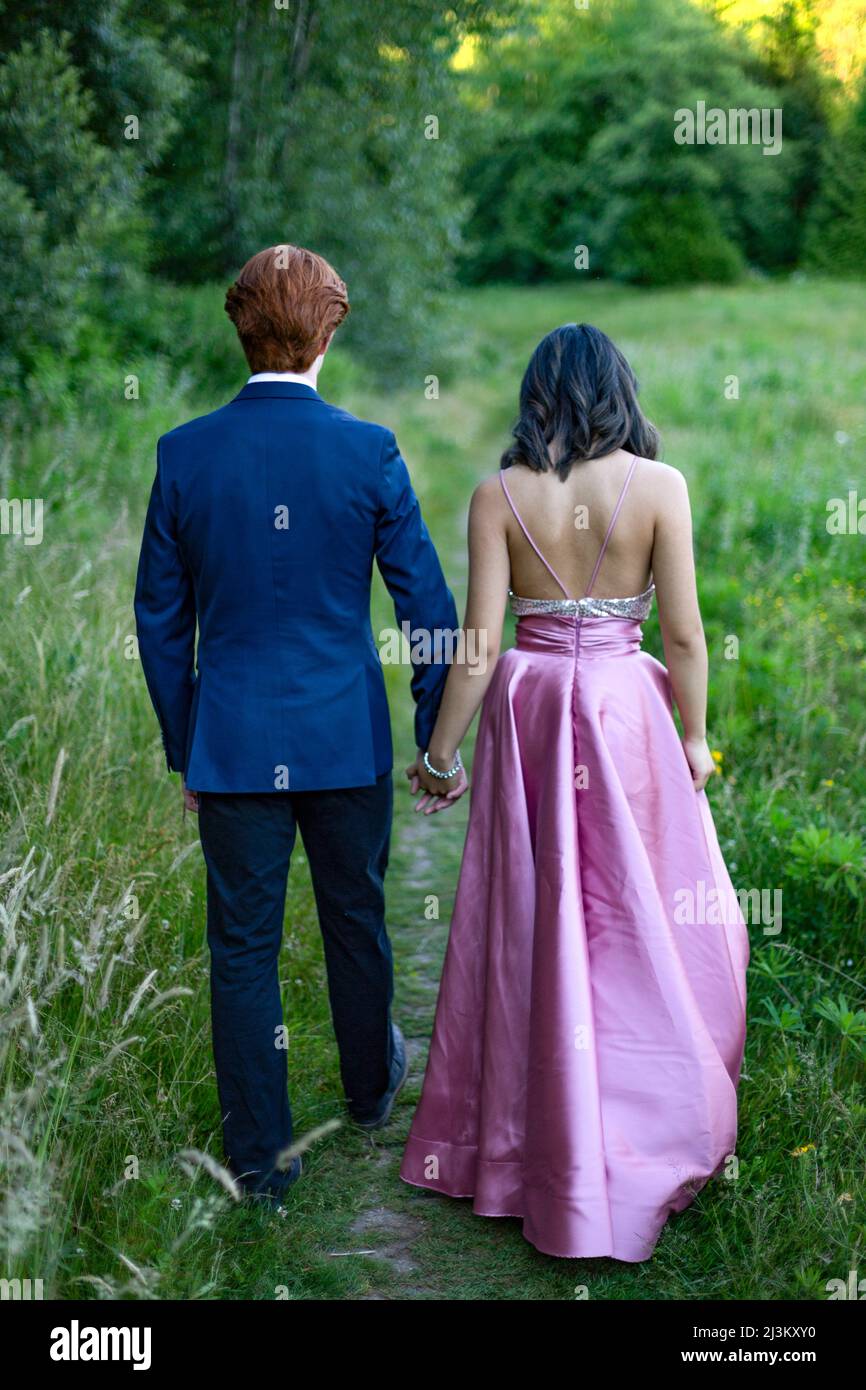 Young couple walking in formal wear down a worn path in a park area ...