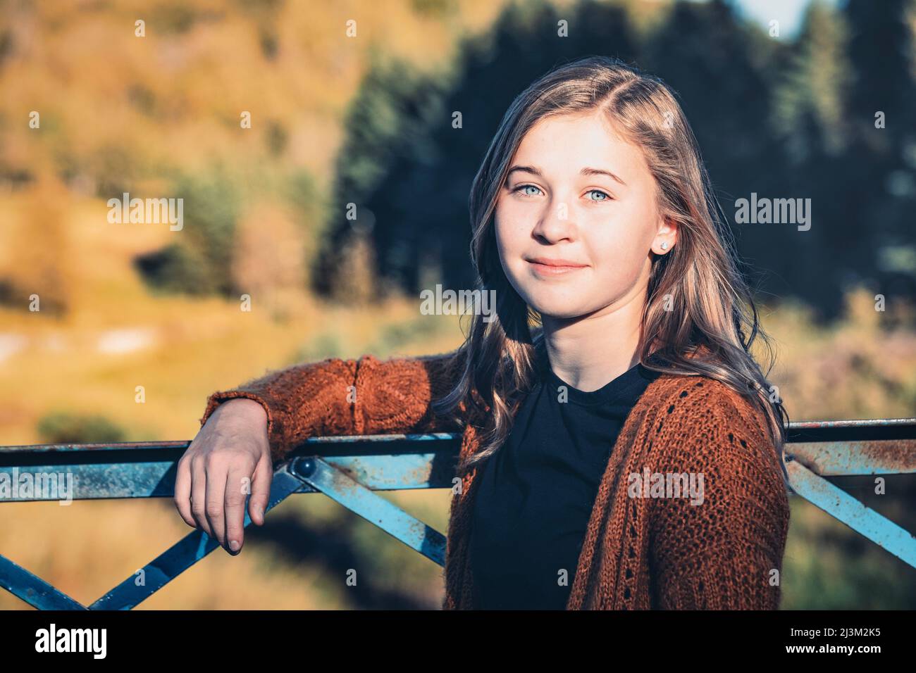 Teenage girl stands outdoors on a park bridge looking at the camera ...