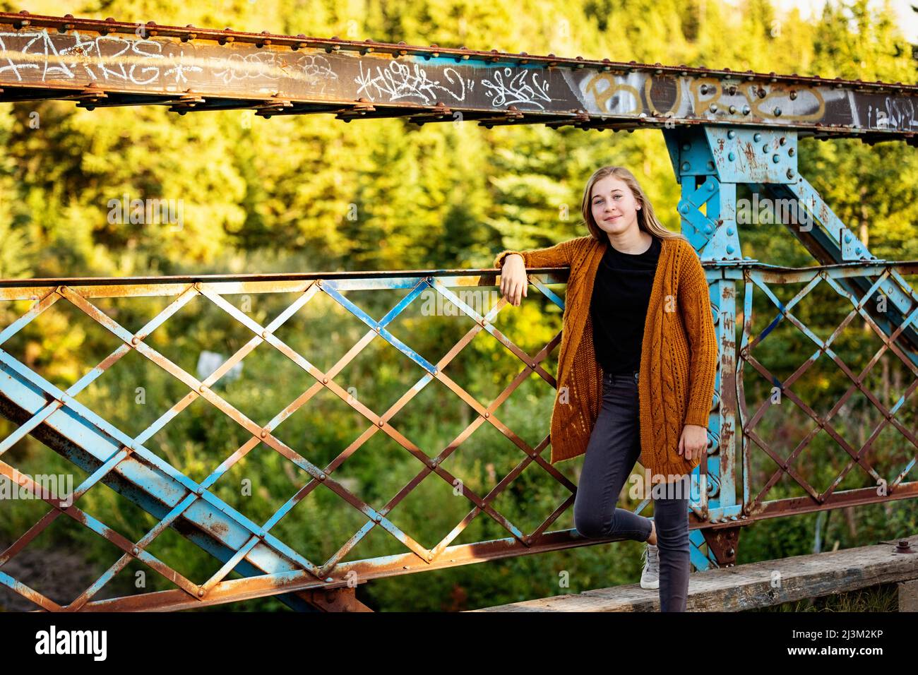 Teenage girl stands outdoors on a park bridge looking at the camera ...