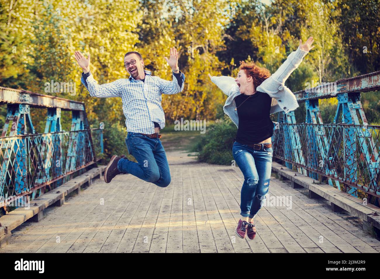 Mature married couple outside in a park leaps in mid-air in exuberant ...