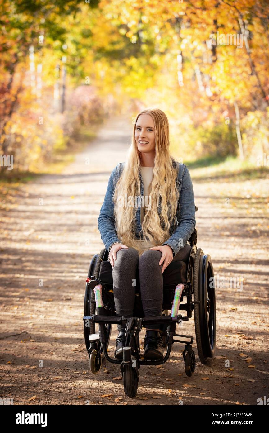 Young paraplegic woman in her wheelchair going down a trail in a park ...