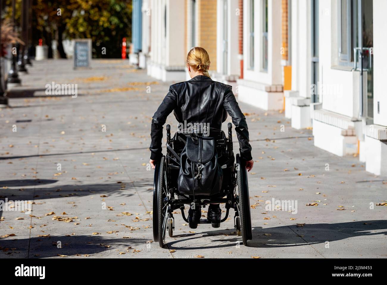 Young paraplegic woman in her wheelchair going down a city walkway on a ...