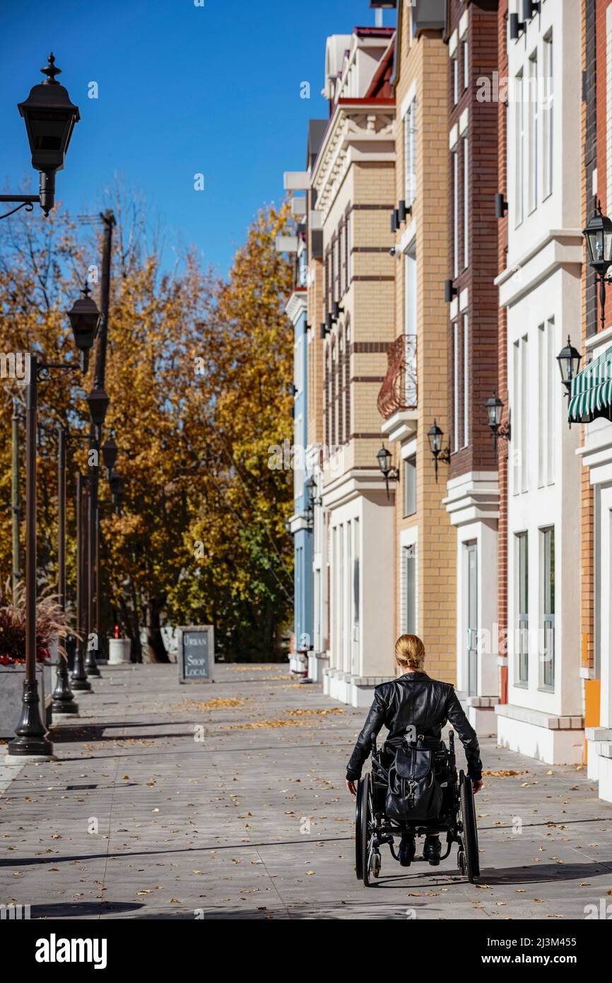 Young paraplegic woman in her wheelchair going down a city walkway on a ...