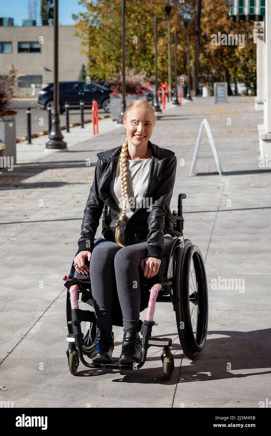 Young paraplegic woman in her wheelchair on a city walkway on a ...